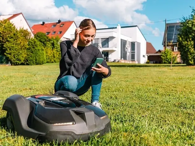 Žena nastavuje robotickou sekačku pomocí mobilní aplikace na trávníku