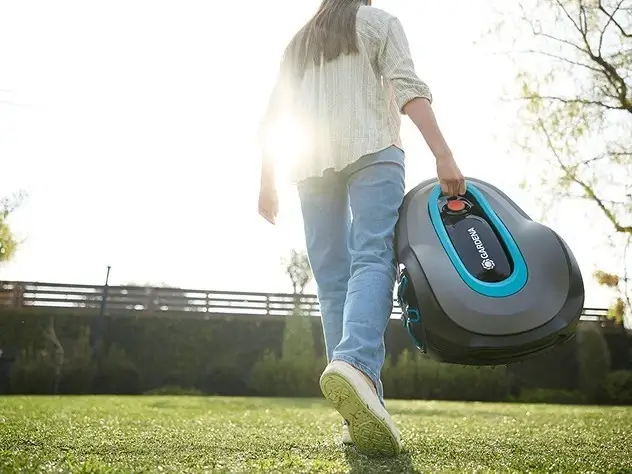 Žena přenáší robotickou sekačku přes trávník